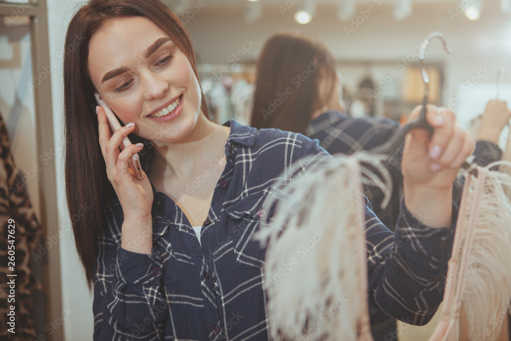 Attractive cheerful female customer talking on the phone while shopping ...