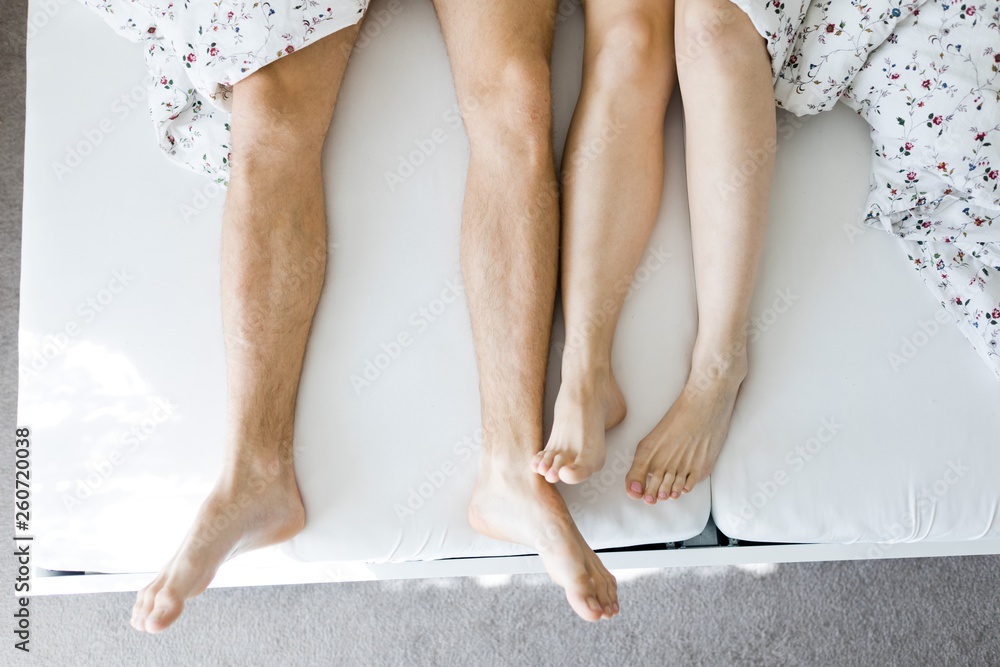 Man's and woman's legs on white sheet of bed partially covered by duvet ...