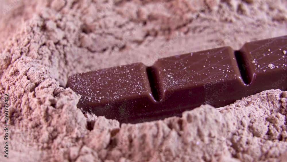 Milk sweet chocolate bar falling in slow motion over chocolate powder ...