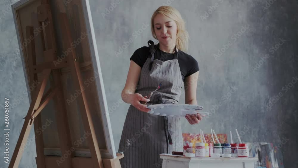 Cheerful woman creates artwork. She painting pictures in modern loft ...