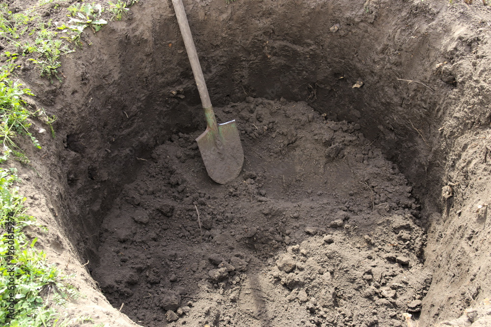 Deep pit in the ground. In the pit lies a shovel. Digging a hole foto ...