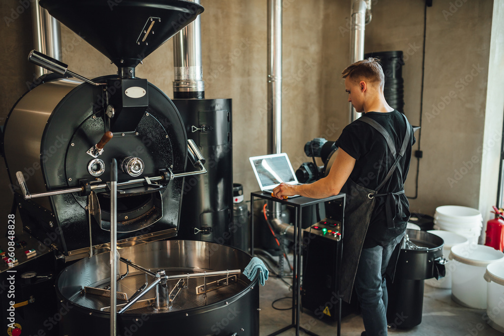 Young man coffee roaster working in roastery, coffee roasting in ...