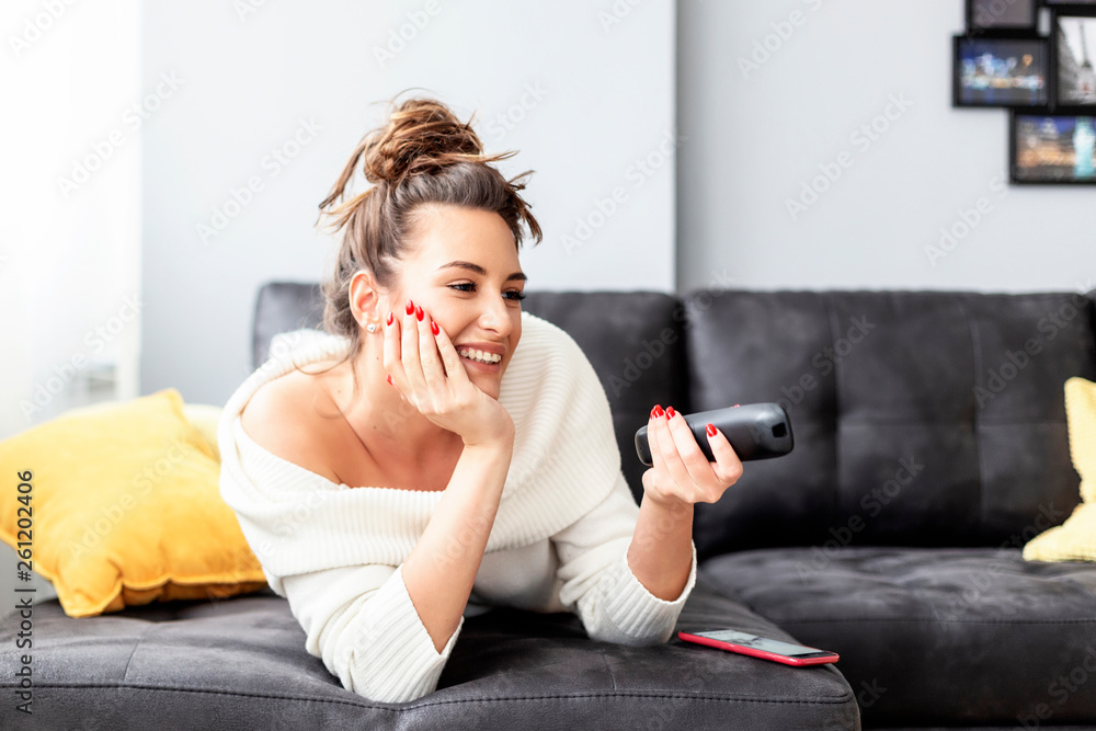 Beautiful girl lying at sofa in room with remote control in her hand ...