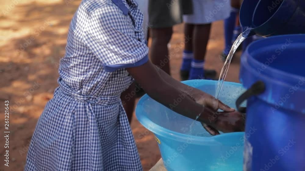 African school pupils wash their hands outside in a plastic dish with ...