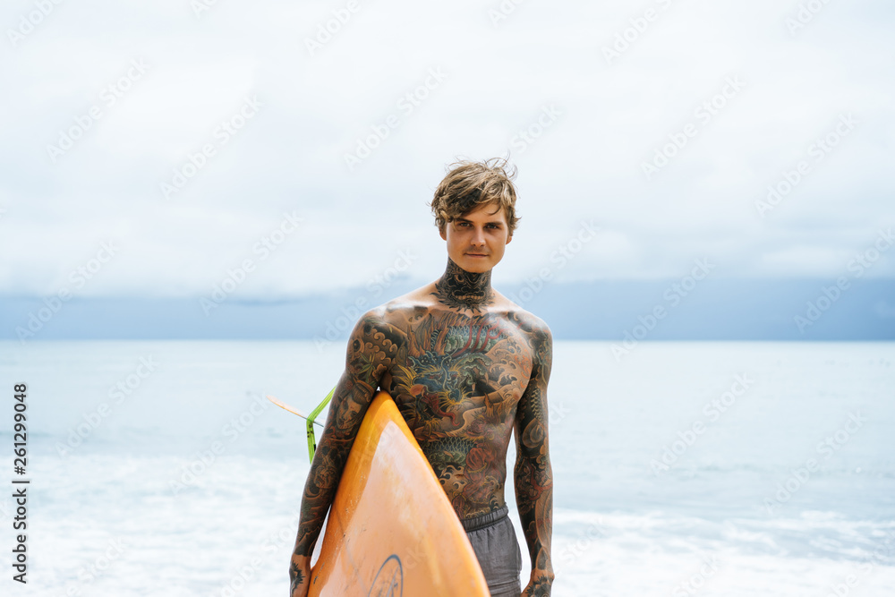 Attractive male surfer in tattoos on the ocean with an orange bright ...