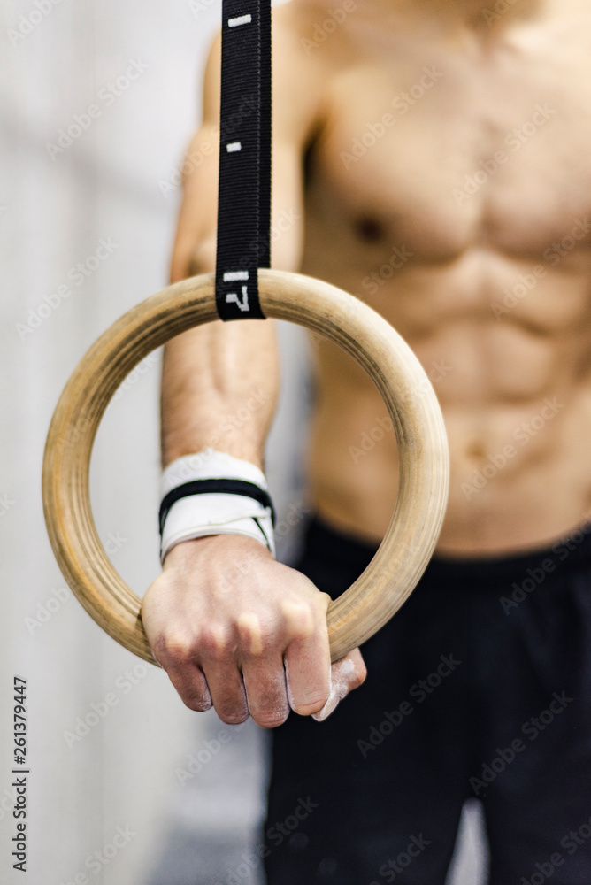 Crop shirtless male with press training with gymnastic rings in gym on ...