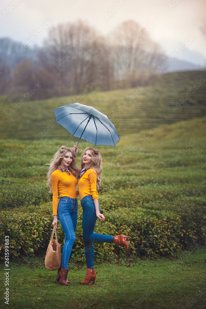Two happy twin girls in yellow under an umbrella walk on tea ...