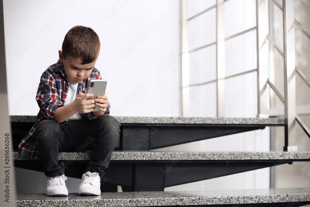 Sad little boy with mobile phone sitting on stairs indoors Stock Photo ...