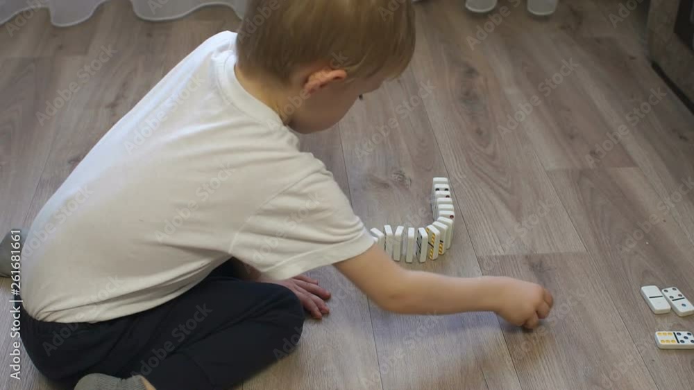 Close-up of a little boy playing dominoes sitting on the wooden floor ...