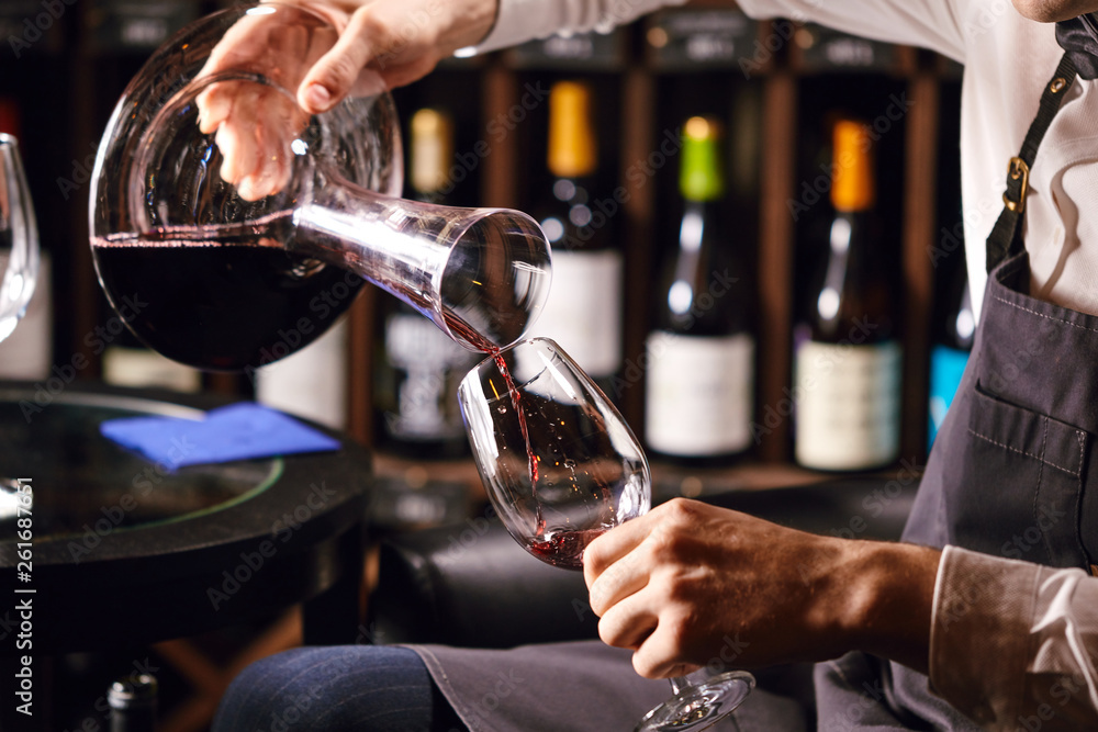 Skilled sommelier pouring wine from decanter into wine glass ...