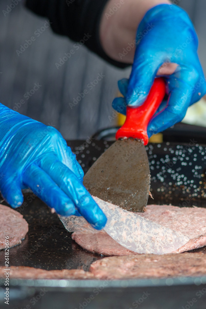 Cooking burgers on a griddle wearing blue gloves to meet food hygiene ...