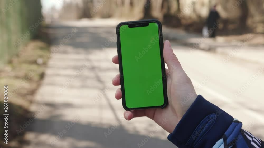 Man holds vertically the green screen smartphone outdoors. Close up man s hand holding and using ...