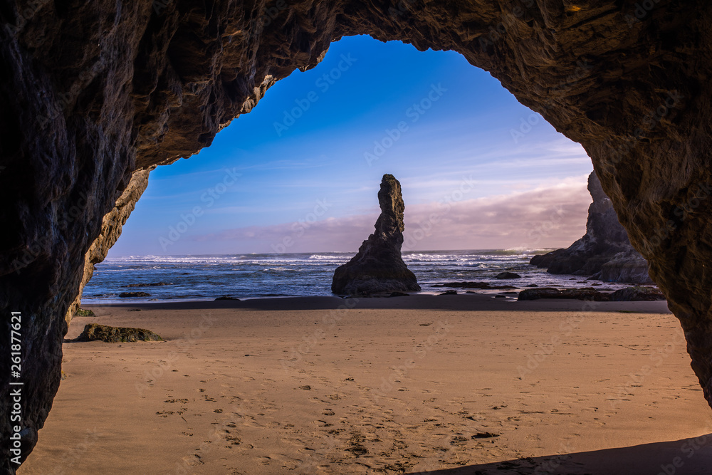 Arch cave at Bandon beach opening in to the ocean. Sea stacks sit ...