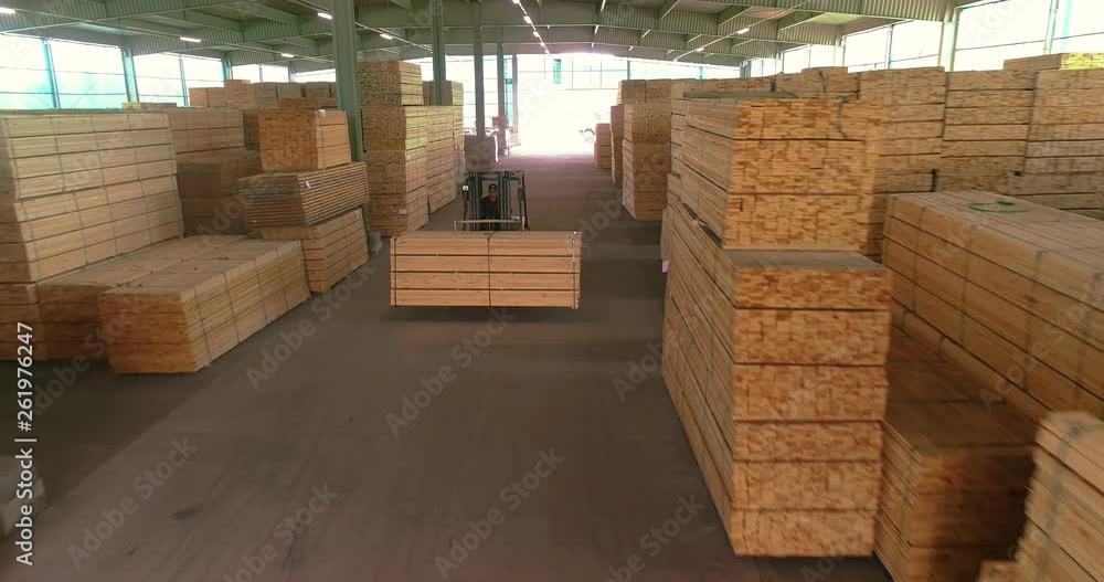 A large warehouse of timber materials. A forklift carries a wooden beam ...