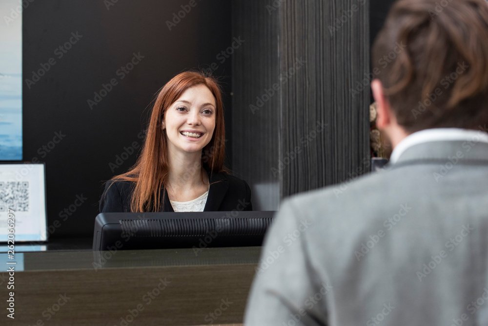 Smiling female receptionist looking at businessman while standing at ...
