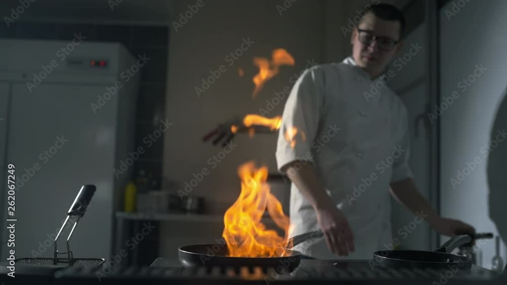 Chef fires up the flambe on a hot pan at the kitchen in slow motion ...