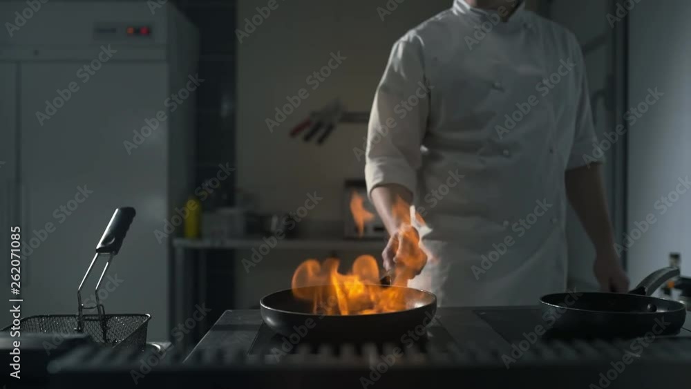 Chef fires up the flambe on a hot pan at the kitchen in slow motion ...