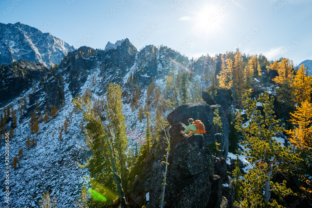 A man with a pack traverses an exposed rocky ridge amidst fall colors ...