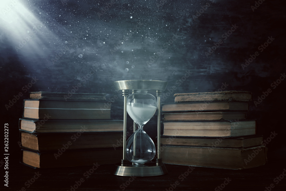 Hourglass as time passing concept and old books in front of black wall ...