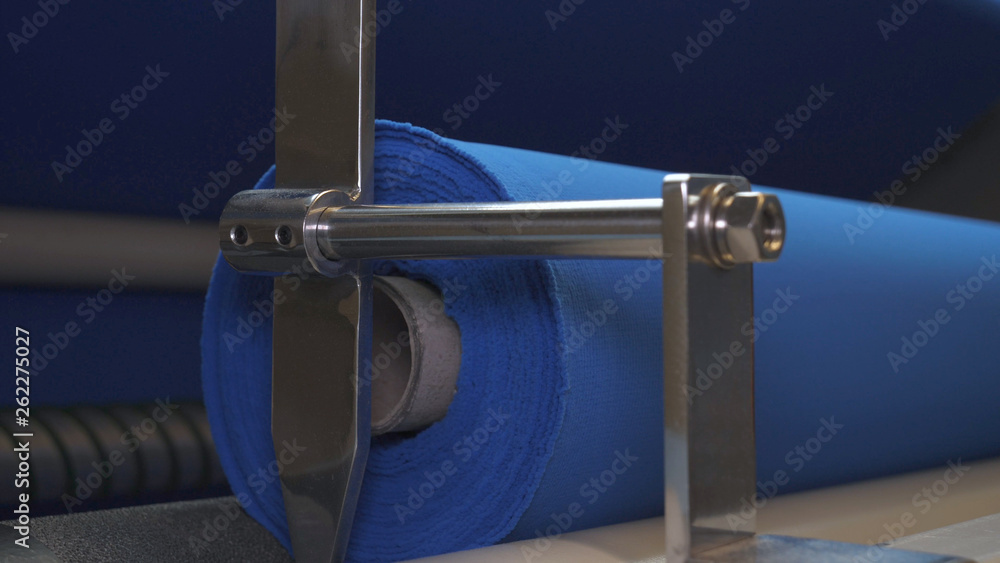 In an industrial garment factory, a roll of blue fabric is wound ...