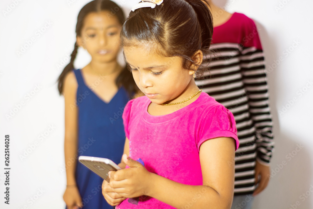 Cute Indian little kid using mobile device and two kids watching the ...