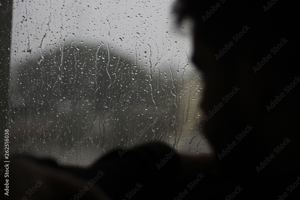 silhouette of a man sitting in the window with rain in mood of sadness ...
