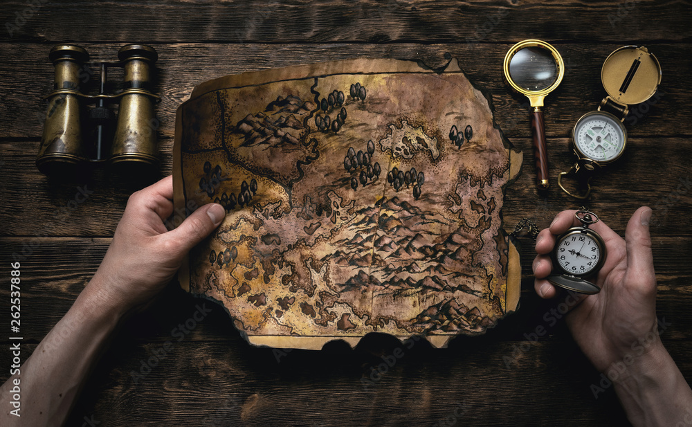 Old map in man adventurer hands on a brown table background. Treasure ...