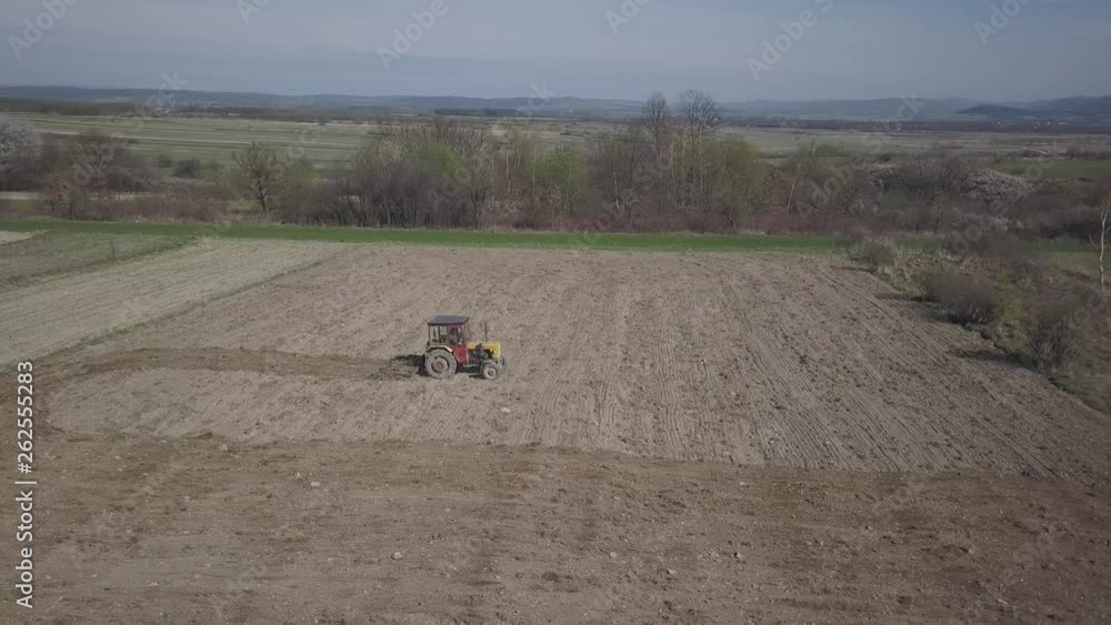 A farmer on a tractor with a seeder sows grain in plowed land in a ...