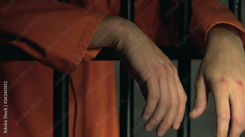 Criminal with beaten hands standing behind prison bars, conflicts in ...