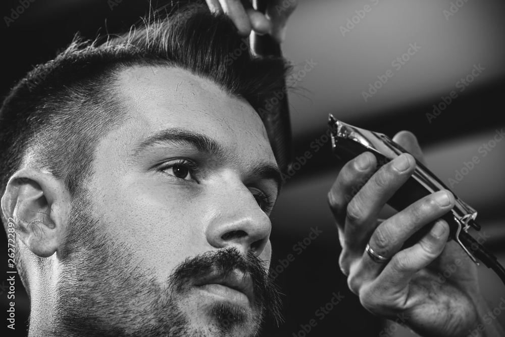 Young handsome barber making haircut for attractive bearded man at ...