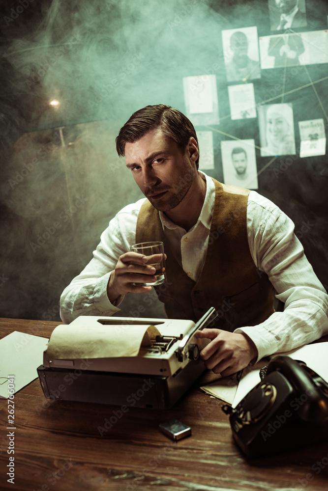 Detective holding glass of cognac while using typewriter in dark office ...