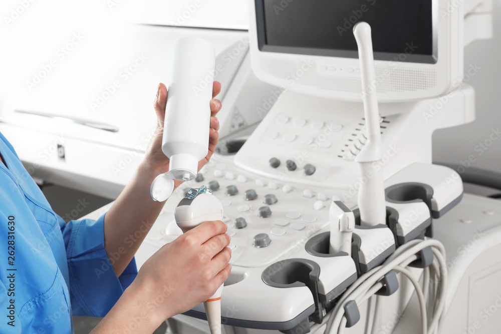 Sonographer covering ultrasound machine probe with gel in clinic ...
