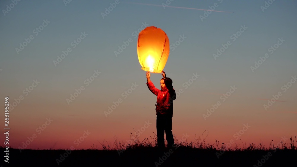 Little child holds lightning chinese sky lantern and release it on red ...