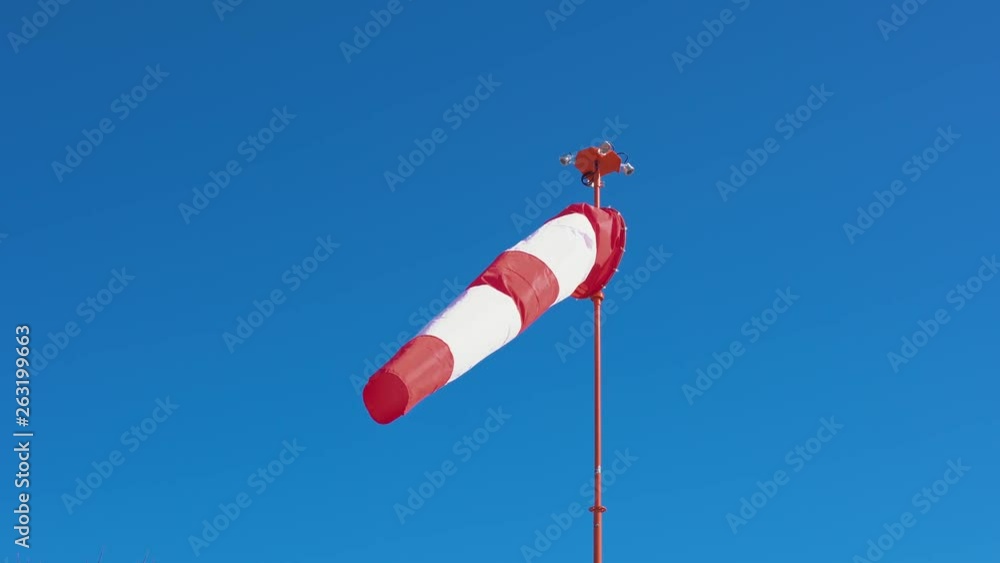 Windsock with red and white stripes develops on blue cloudless sky ...