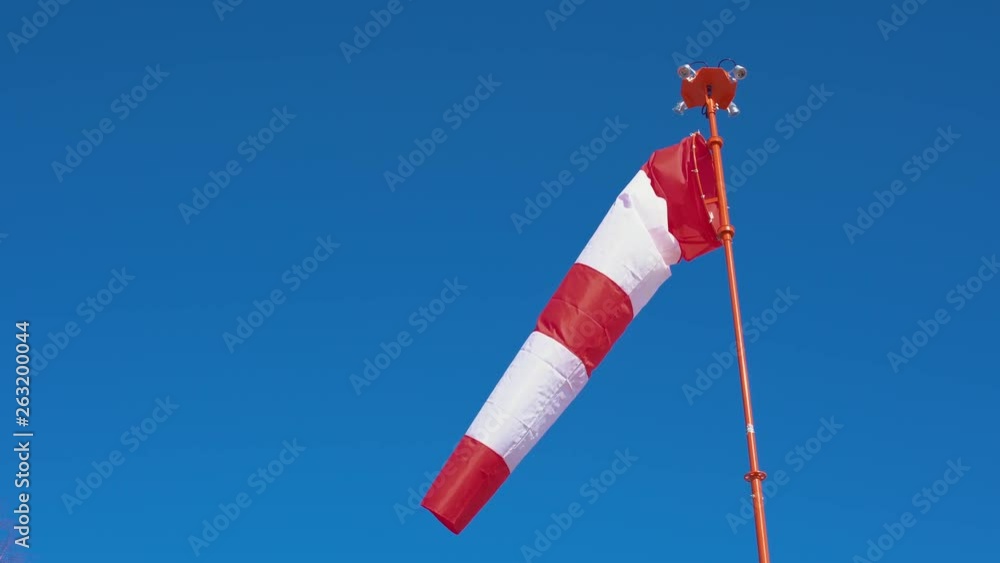 Windsock with red and white stripes develops on blue cloudless sky ...