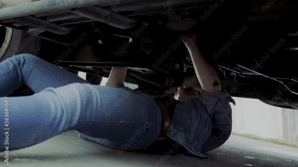 Video Stock Woman in early 20s checking under the hood of a truck and going under the truck to ...