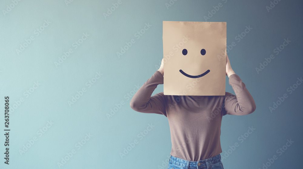 Woman covering his face with a smiling face emoticon, copy space. Stock ...