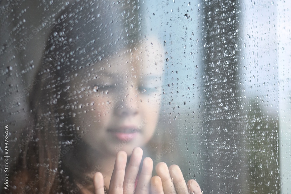 Beautiful toddler girl looking through the window with raindrops and ...