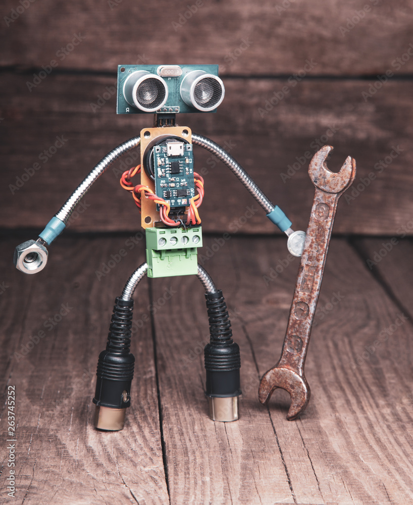 Robot made of parts of circuit boards with wrench, on wood background ...