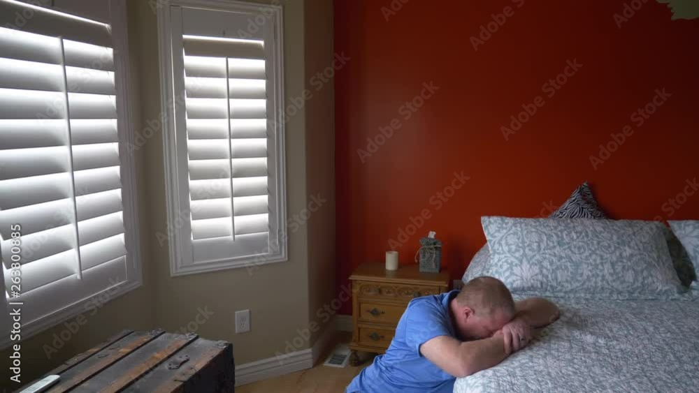 A sad, lonely and depressed man sits on the edge of his bed in despair ...