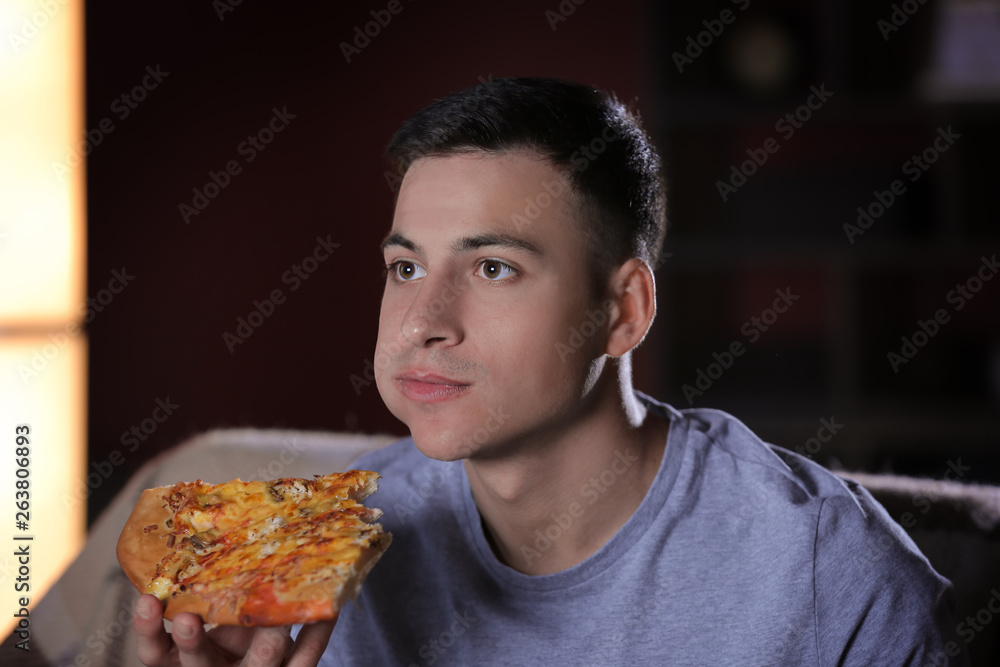 Handsome young man eating unhealthy food while watching TV at night ...