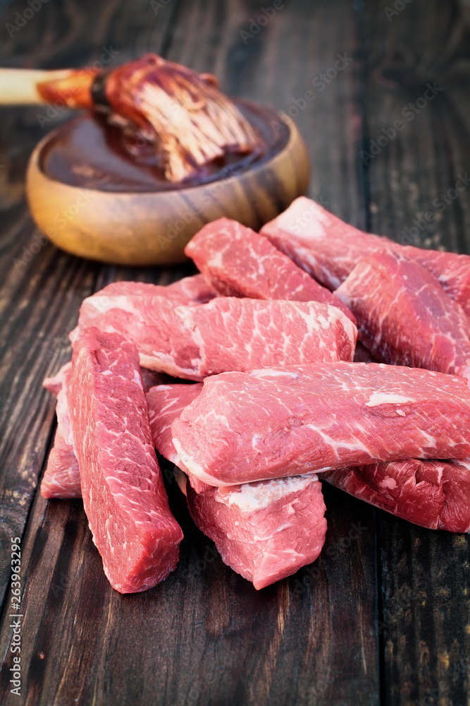Uncooked raw boneless beef ribs with bowl of barbecue sauce and bbq ...