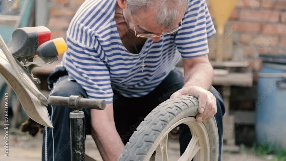 an elderly man repairs his bike in the yard in the village,the old man ...