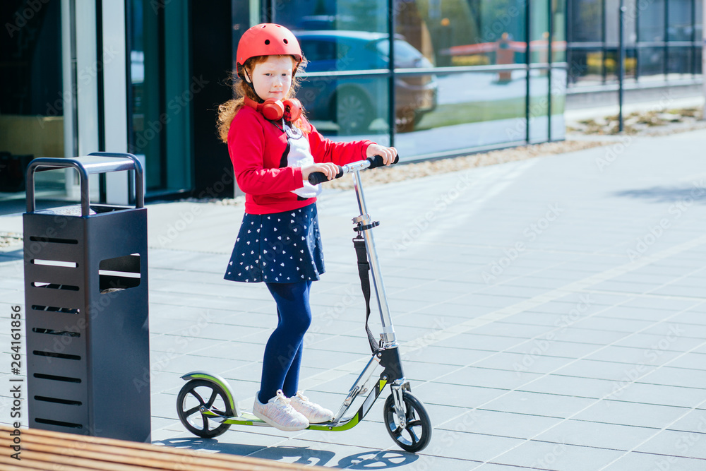 Red hair girl in red helmet riding scooter on way back to school. Kid ...