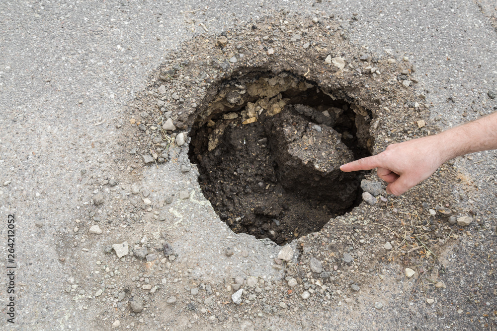 Driver's hand pointing to the big, deep hole on the asphalt road ...