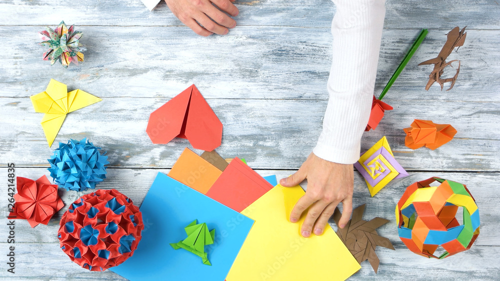 Hands making origami, top view. Wooden table with a lot of origami ...