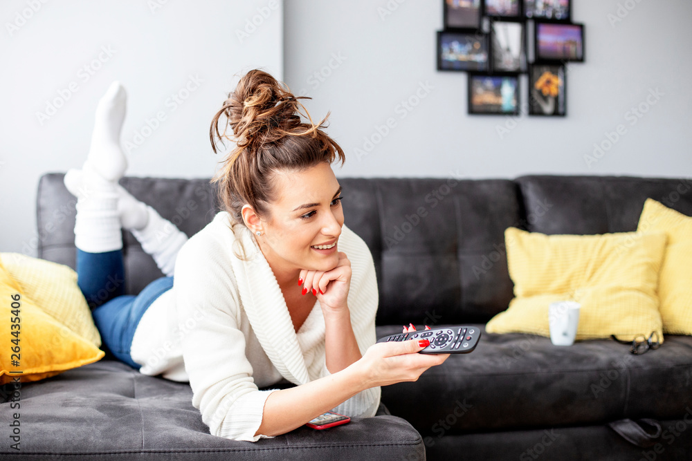 Beautiful girl lying at sofa in room with remote control in her hand ...