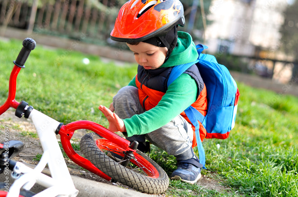 Sports Kid boy in a protective helmet checks his red white balance bike ...