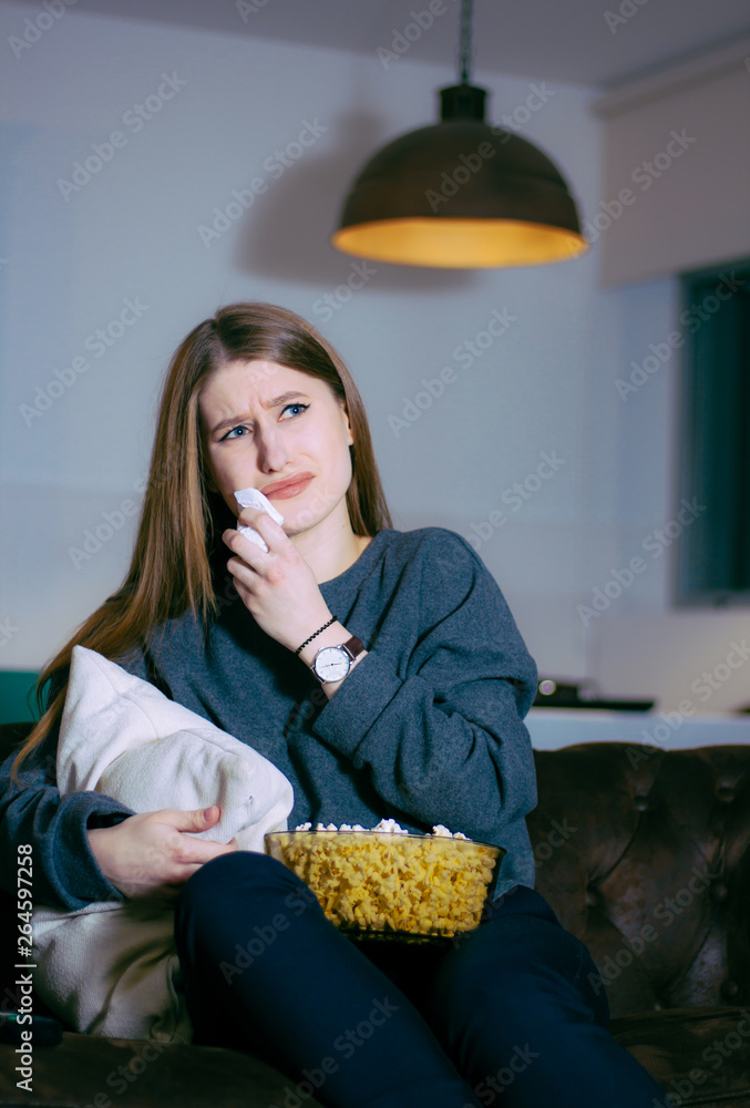 Young woman crying while watching sad movie on the tv at home. Shie is ...