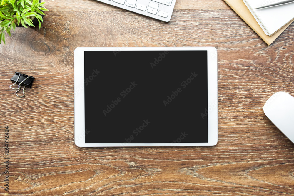 White tablet with black blank screen is on top of wood desk table with ...
